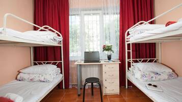 Quarto de dormitório com duas camas beliche, uma escrivaninha com um laptop, um banquinho pequeno e uma janela com cortinas.