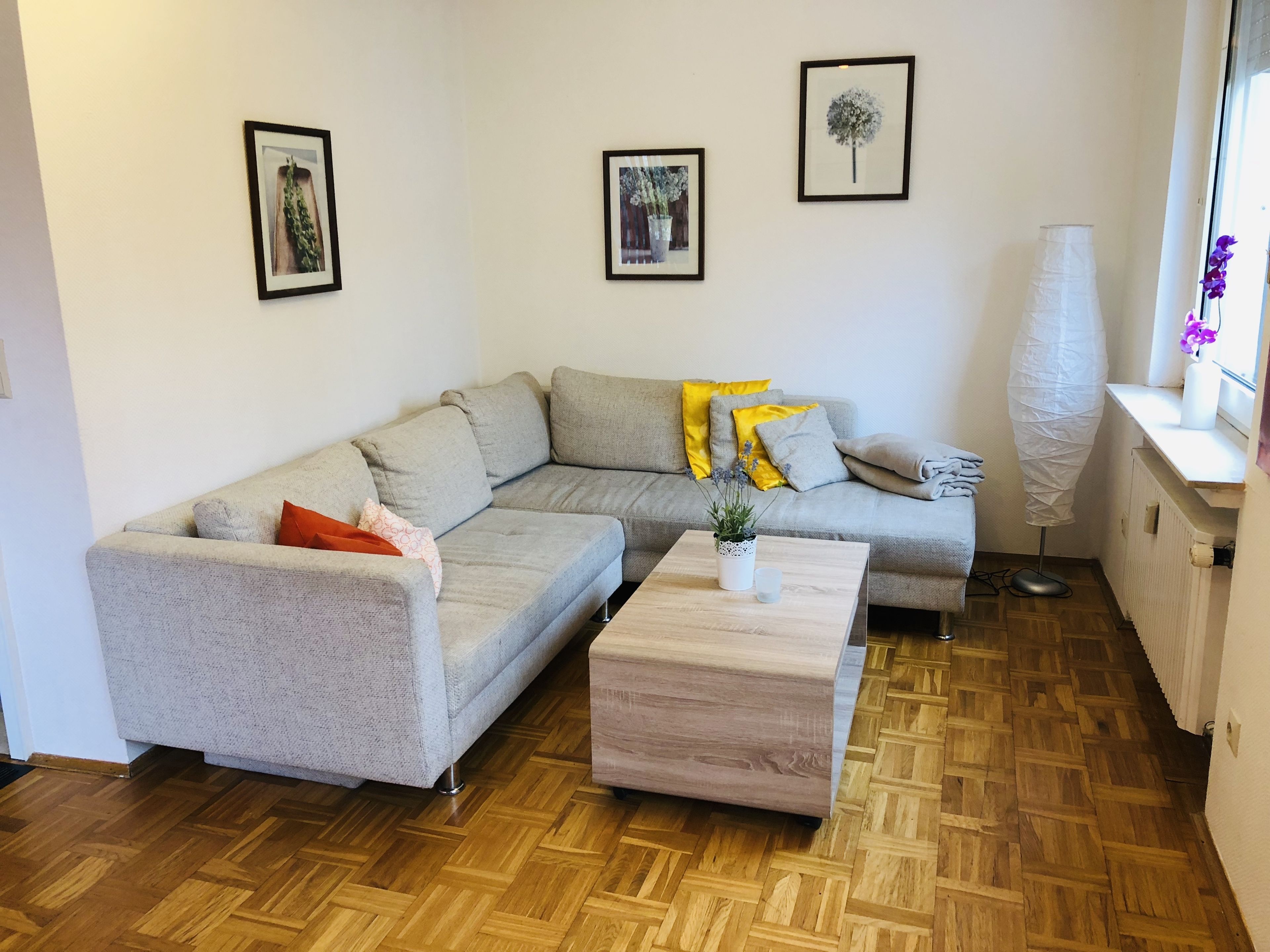 Uma sala de estar moderna com um sofá modular cinza, uma mesa de centro de madeira e um piso com padrão espinha de peixe.