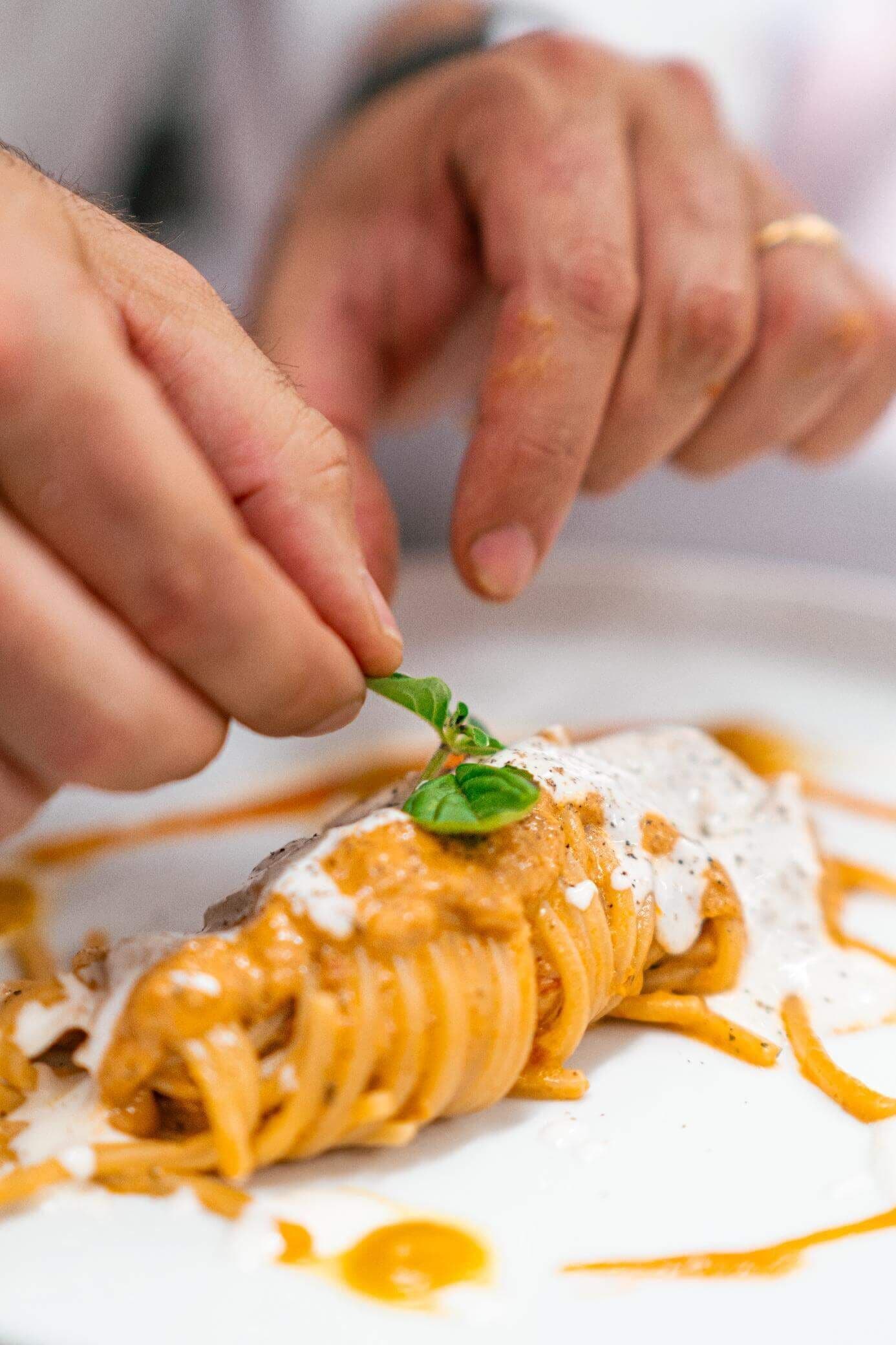 Um close-up de uma mão segurando um pedaço de comida, possivelmente uma sobremesa, com molho cremoso e um enfeite.