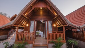 Uma cabana de madeira com telhado triangular, varanda frontal e escadaria que leva à entrada.