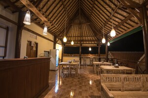 Um interior rústico de madeira com teto alto, mesas e bancos de madeira e luminárias pendentes.