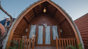 Uma cabana de madeira com telhado inclinado, varanda com guarda-corpo e uma porta grande com painéis de vidro.