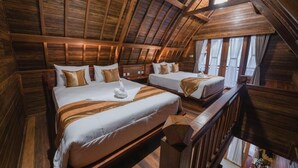 Um quarto de sótão acolhedor, com vigas de madeira, duas camas e janelas amplas.