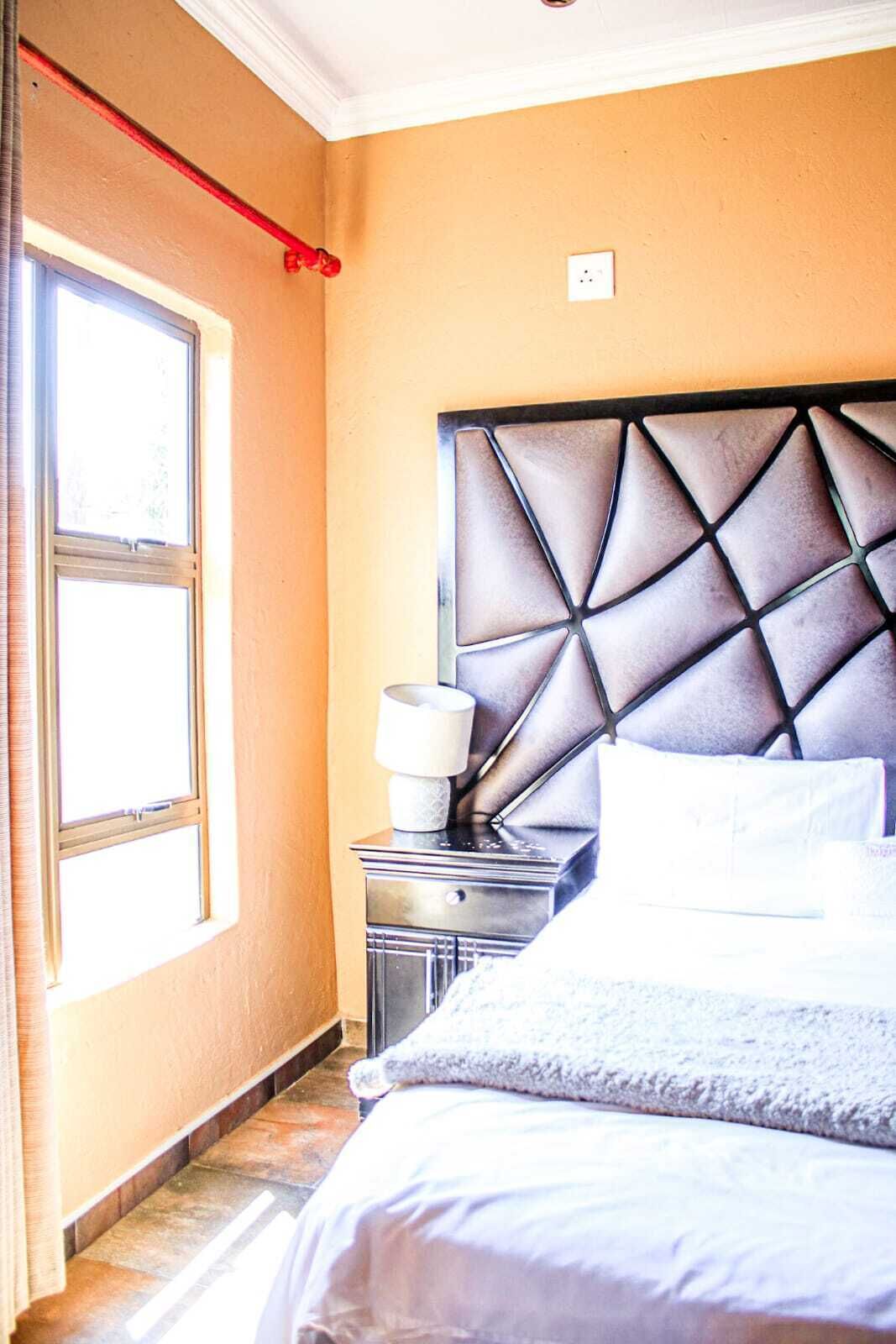 Quarto com cama, mesa de cabeceira com luminária, janela e tomada na parede.