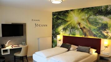 Quarto de hotel moderno com cama, escrivaninha, cadeira e um grande mural com tema de árvore na parede.