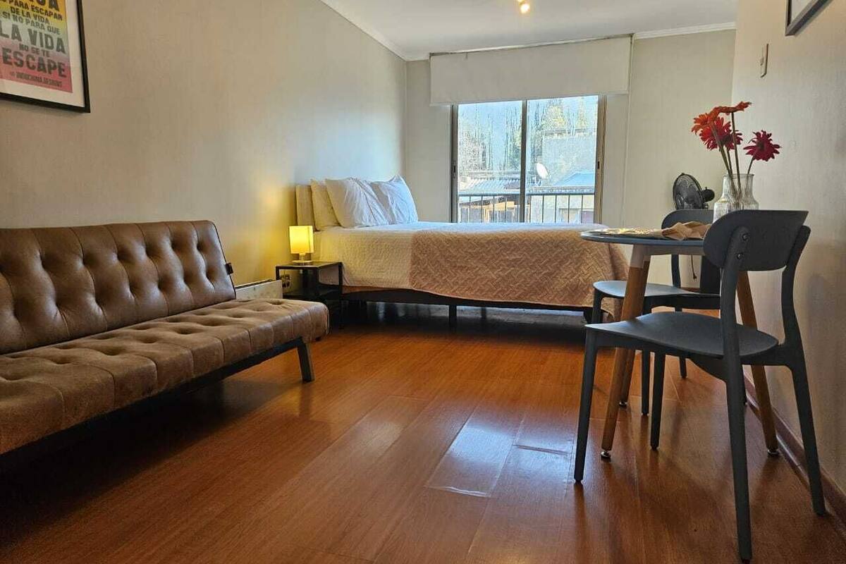 Quarto com cama, sofá, cadeira, mesa de cabeceira e janela.