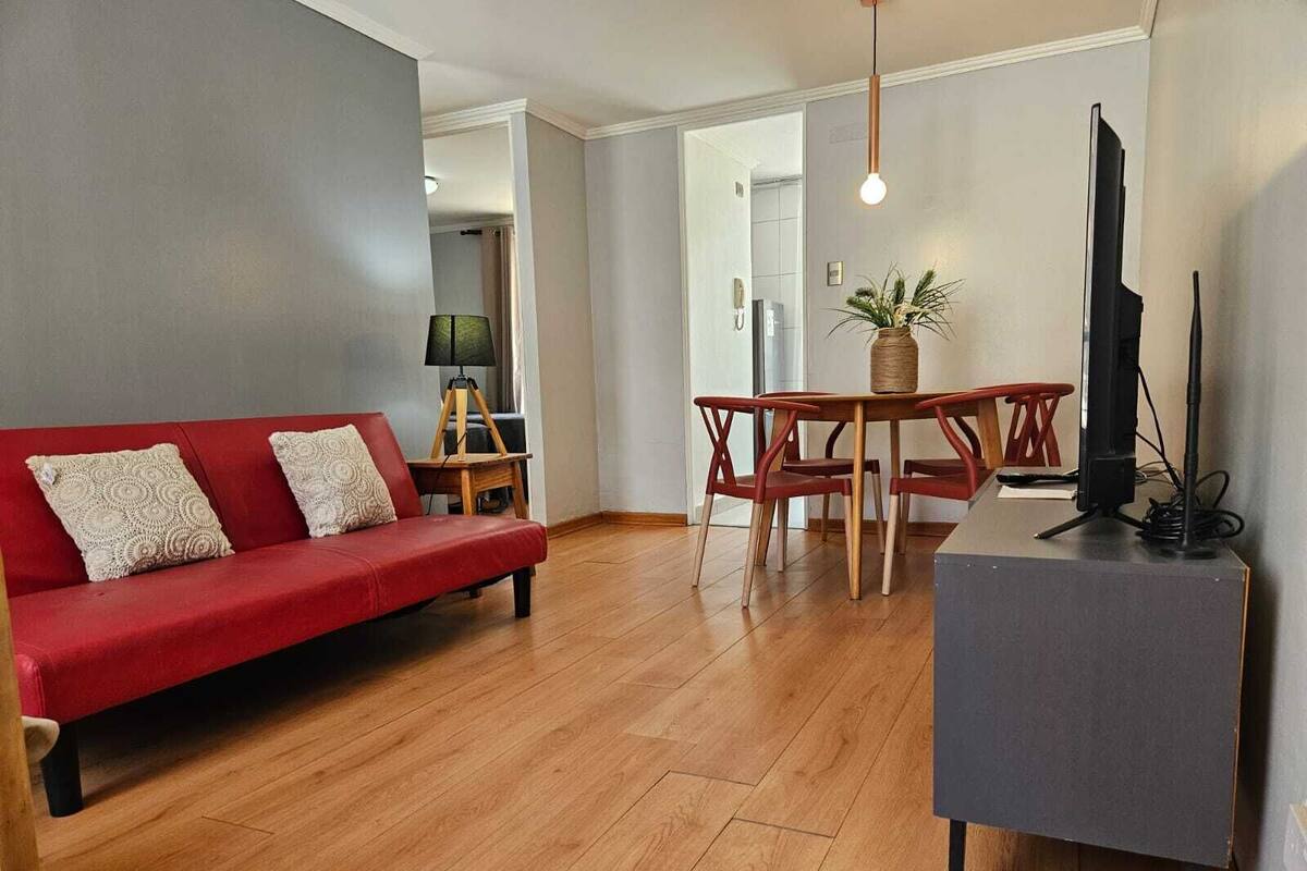 Uma sala de estar com um sofá vermelho, mesa de jantar de madeira e uma televisão em um móvel.