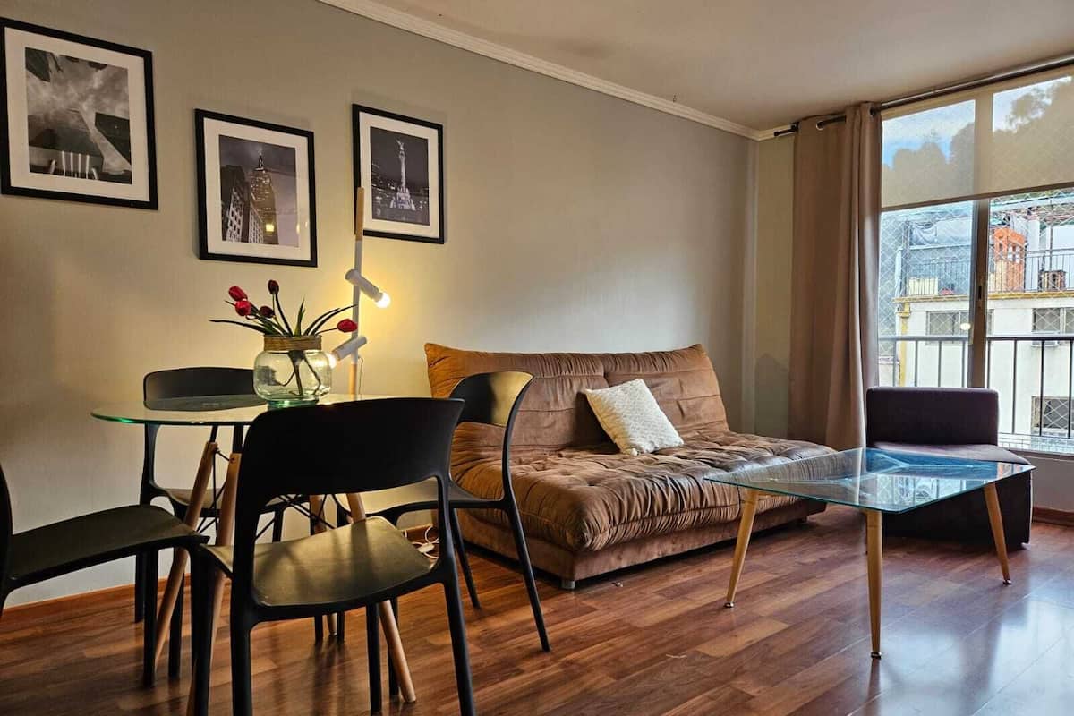 Uma sala de estar moderna com uma mesa de centro de vidro, um sofá, uma mesa de jantar com cadeiras e quadros nas paredes.