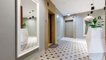 Um corredor moderno com piso estampado, um espelho grande, uma planta em vaso e uma porta com o símbolo de número.