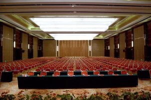 Uma sala de conferências com fileiras de cadeiras, uma mesa comprida e piso coberto de carpete.