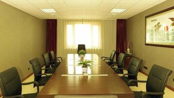 Uma sala de conferências com uma mesa comprida, cadeiras, uma planta e um quadro na parede.