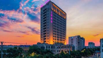 Um hotel moderno com vários andares, uma entrada imponente e vista para a paisagem urbana ao redor.