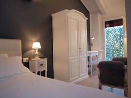 Quarto com cama, mesa de cabeceira com luminária, guarda-roupa, cadeira e vista para o verde através de uma janela.
