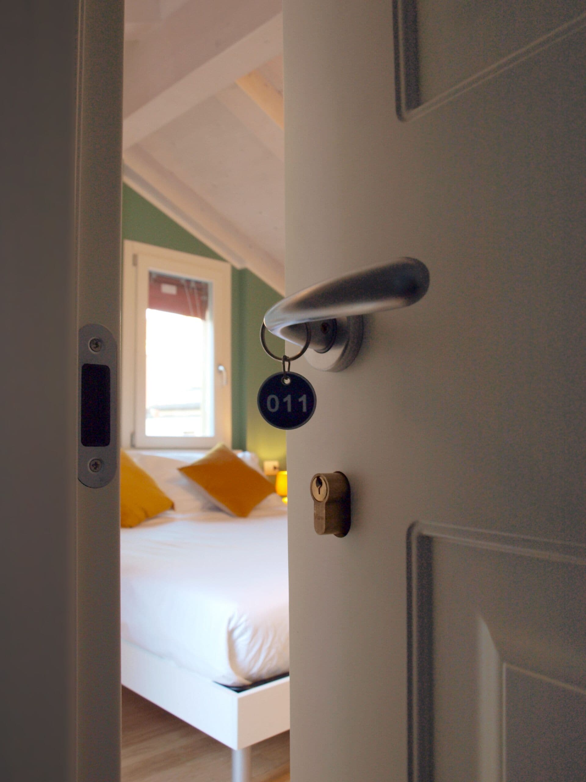 Quarto com uma cama, porta com olho de fechadura e placa de número na porta.