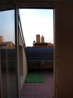 Vista de uma varanda com um tapete verde, com vista para um horizonte urbano com edifícios bem definidos e céu claro.