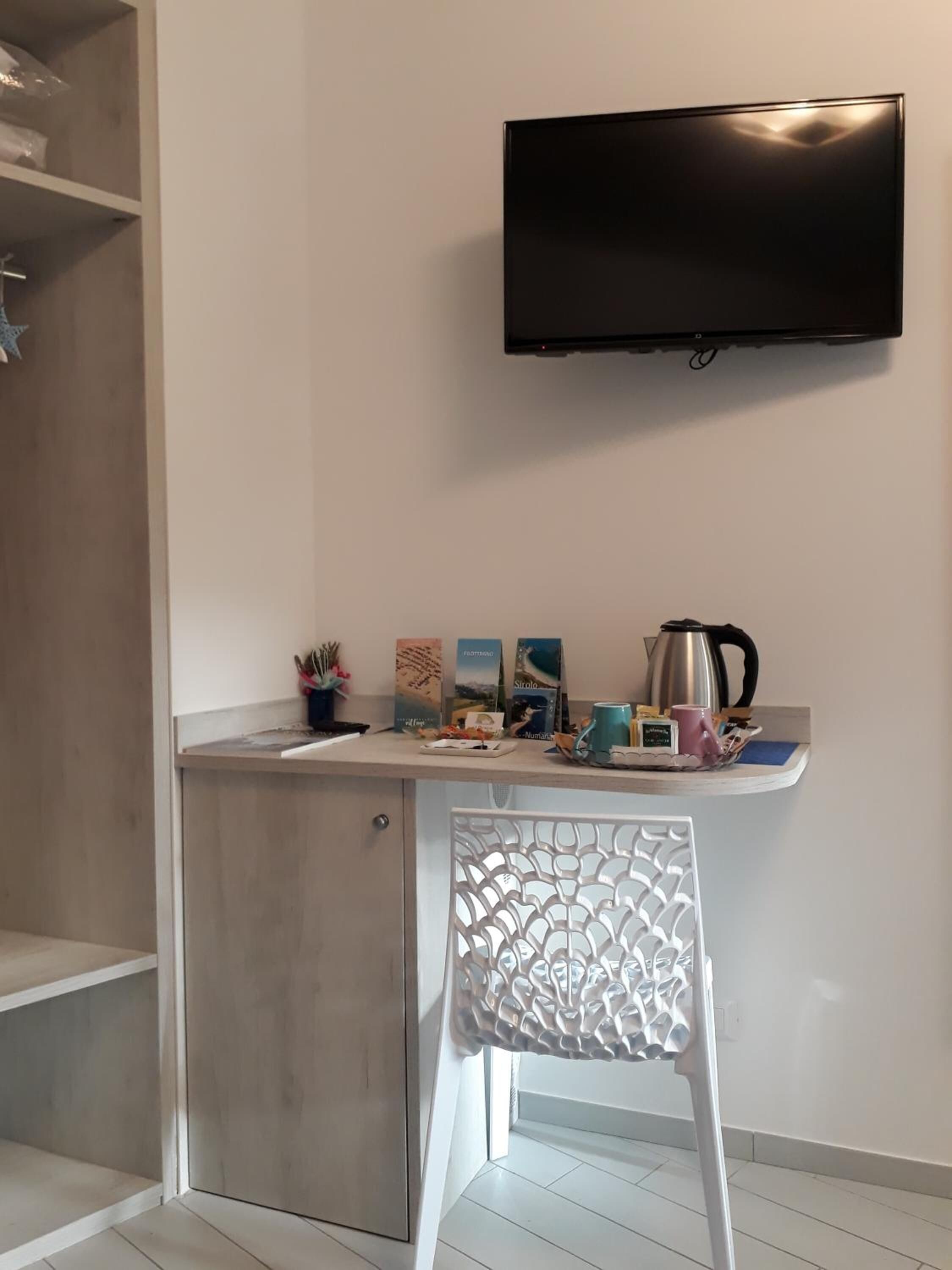 Uma cozinha compacta com televisão de tela plana presa acima de uma bancada, uma cafeteira e diversos objetos sobre a bancada.