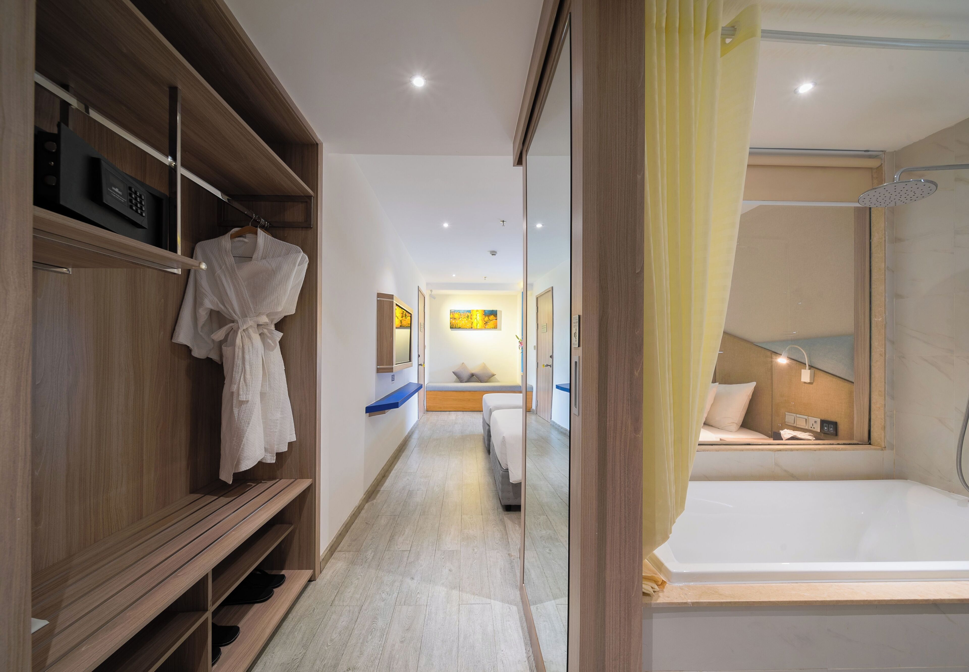 Quarto de hotel moderno com closet espaçoso, cama grande, banheiro separado com chuveiro e mesa de cabeceira com abajur.