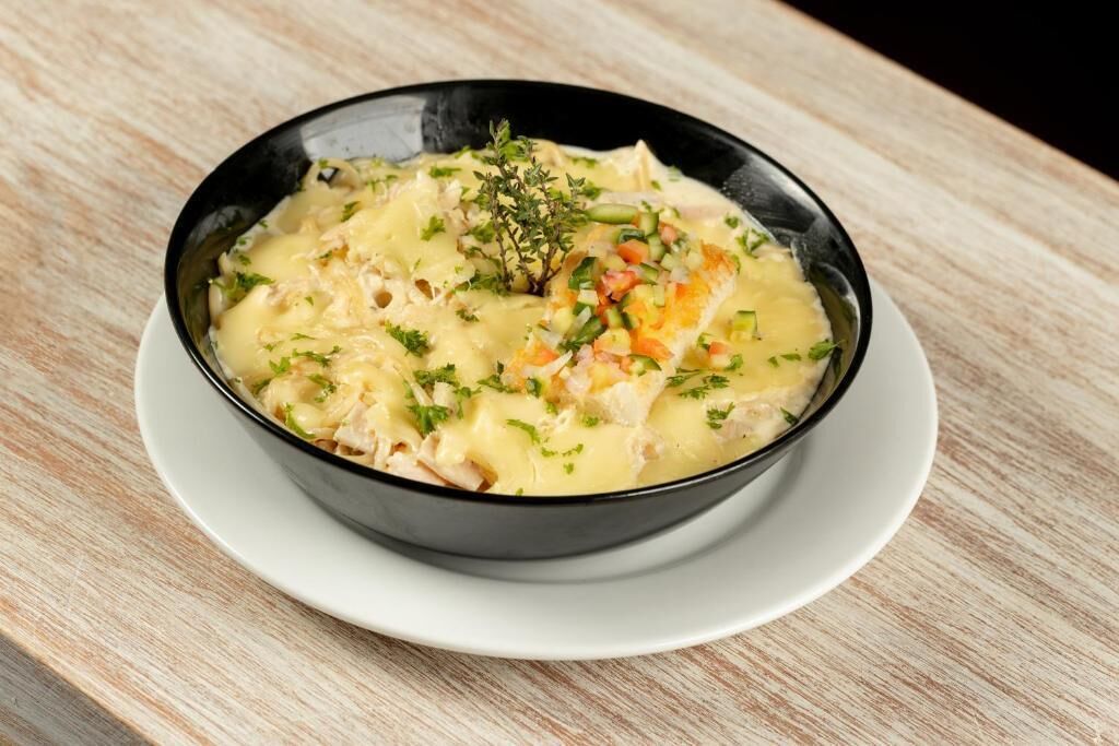 Uma tigela de sopa com legumes e ervas sobre um prato branco.