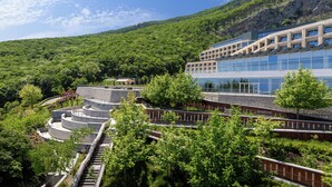 Um hotel moderno com área externa em terraços, cercado por vegetação exuberante e montanhas ao fundo.