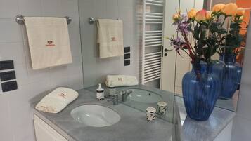Casa de banho com lavatório, espelho, toalhas e um vaso com flores.