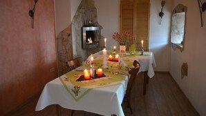 Uma sala de jantar com lareira de pedra, persianas de madeira e uma mesa posta com velas e flores.