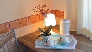 Uma mesa de madeira com uma lâmpada, um pequeno vaso de planta e um tabuleiro com chávenas e uma caixa de lenços.