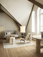 Quarto de loft acolhedor com vigas de madeira aparentes, uma janela grande, um sofá, uma poltrona, uma mesa e um abajur.