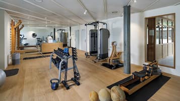 Uma academia ampla com diversos equipamentos de exercícios, incluindo uma máquina de remo, kettlebells e um suporte para pesos.