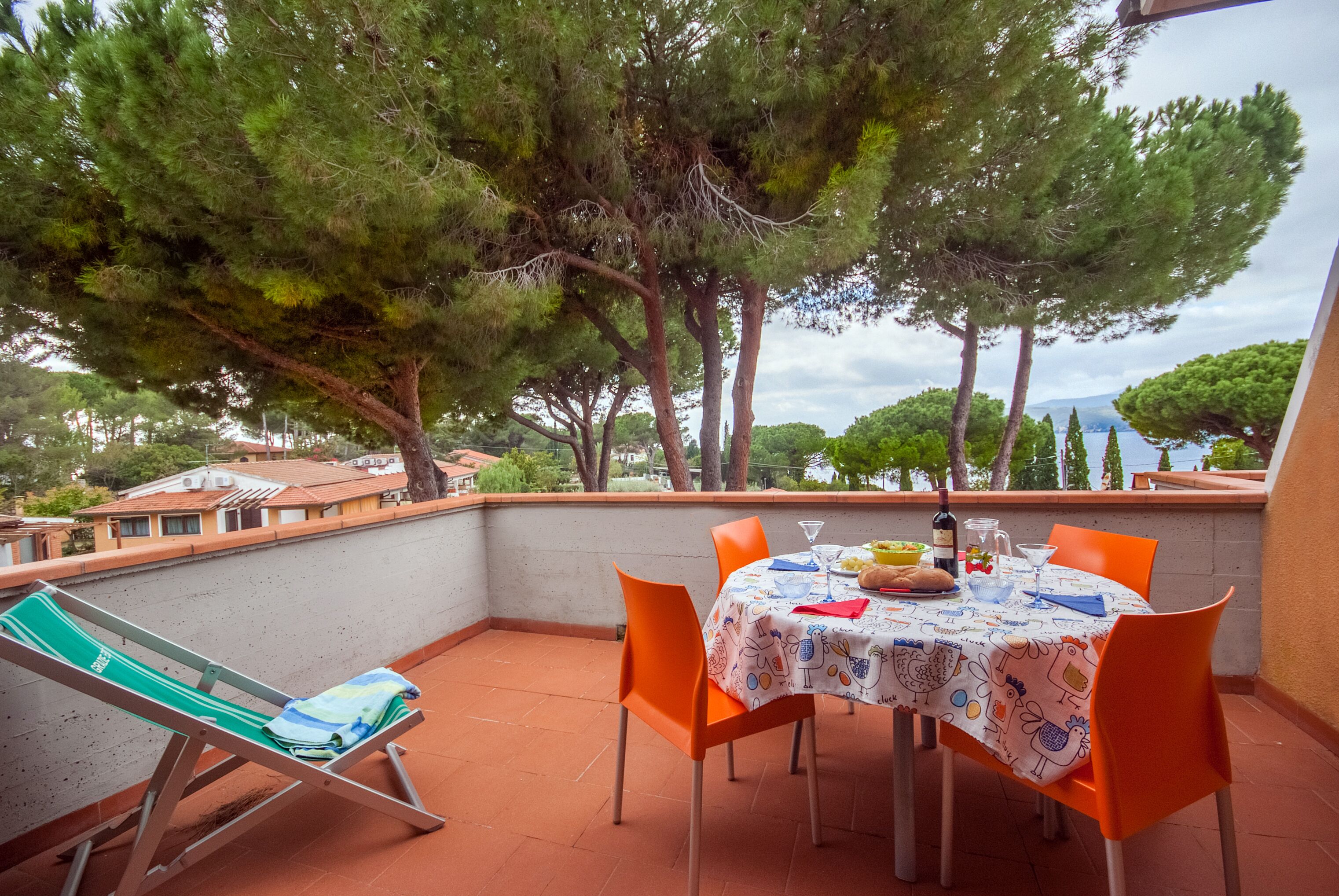 Um terraço com uma mesa posta para refeições, cercado por cadeiras laranjas e uma poltrona.