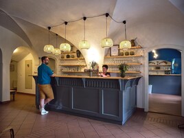 Uma área de bar com balcão, luminárias de vime suspensas, prateleiras com copos e garrafas, e uma parede azul de destaque.