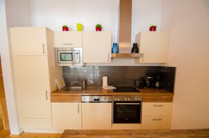 Cozinha compacta com micro-ondas, fogão, forno e pia. Há armários e uma bancada com alguns objetos.