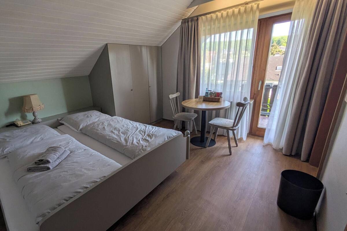Quarto com duas camas, uma mesa pequena com cadeiras e vista para o exterior através de uma janela.
