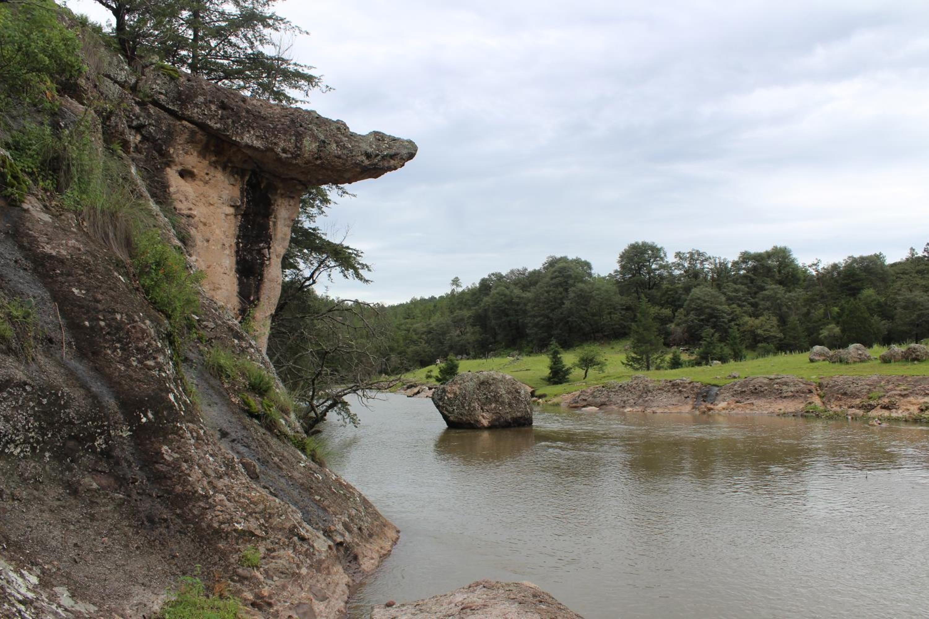 Paisagem natural com rio, falésias rochosas e área arborizada.