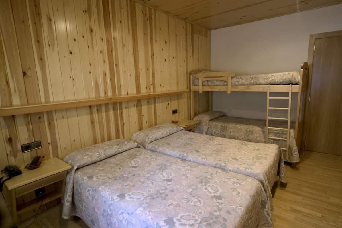Quarto com paredes de madeira e uma cama beliche. Há uma mesa de cabeceira com uma lâmpada e um telefone.