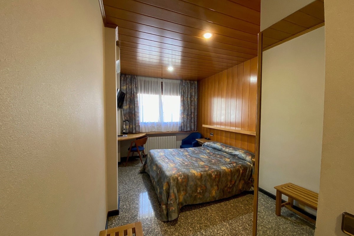 Quarto pequeno com uma cama, uma escrivaninha e uma cadeira.