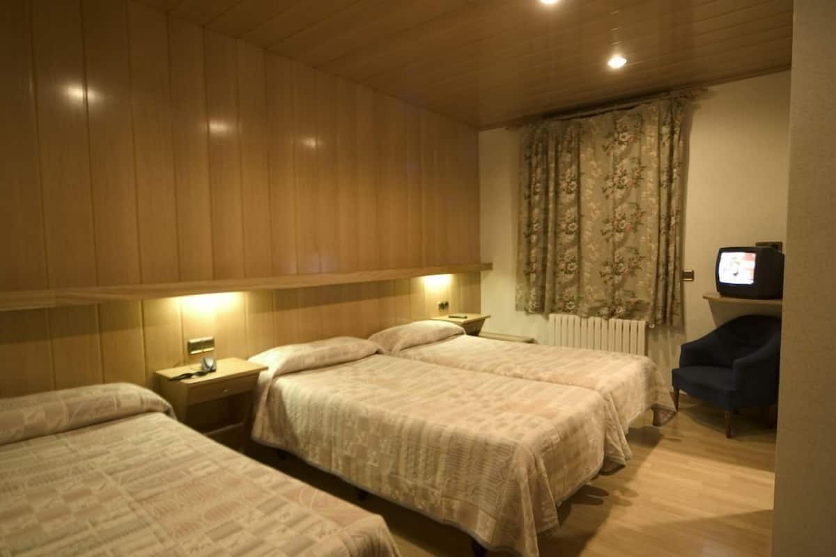 Quarto de hotel com duas camas, painéis de madeira nas paredes, televisão e janela com cortinas.
