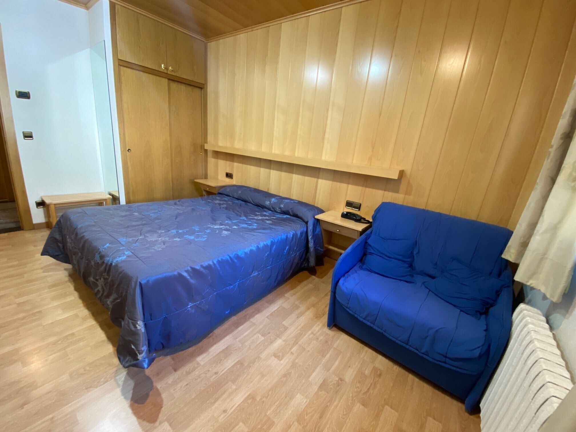 Quarto com cama, sofá azul, paredes de madeira e chão de madeira.