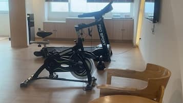 Um quarto com piso de madeira, uma mesa de jantar com cadeiras e duas bicicletas ergométricas.
