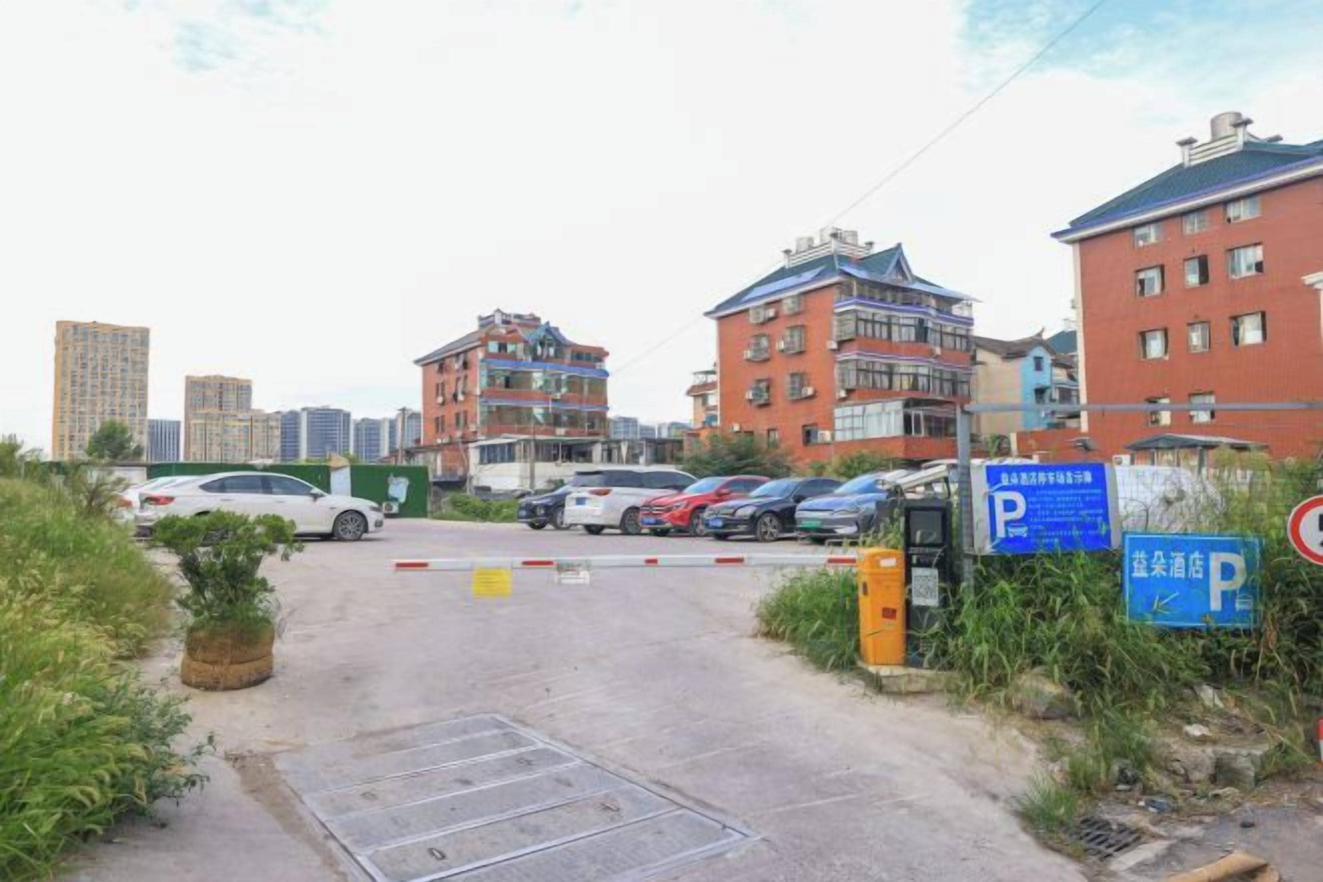 Área de estacionamento fechada com vários carros, uma placa de estacionamento azul e edifícios ao fundo.