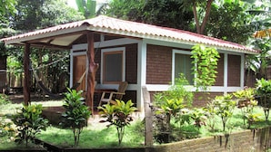 Uma casa de dois andares com telhado vermelho, varanda de madeira e fachada de tijolos.