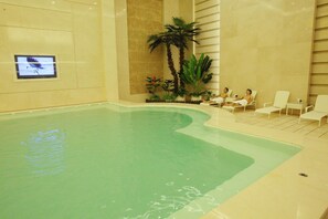 Piscina interna com espreguiçadeiras e plantas de palmeira.