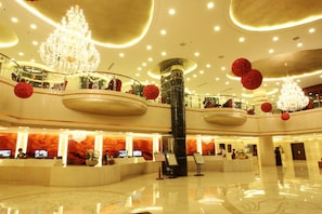 Um hall de hotel em vários níveis, com um lustre imponente, um balcão de recepção e decorações esféricas vermelhas.