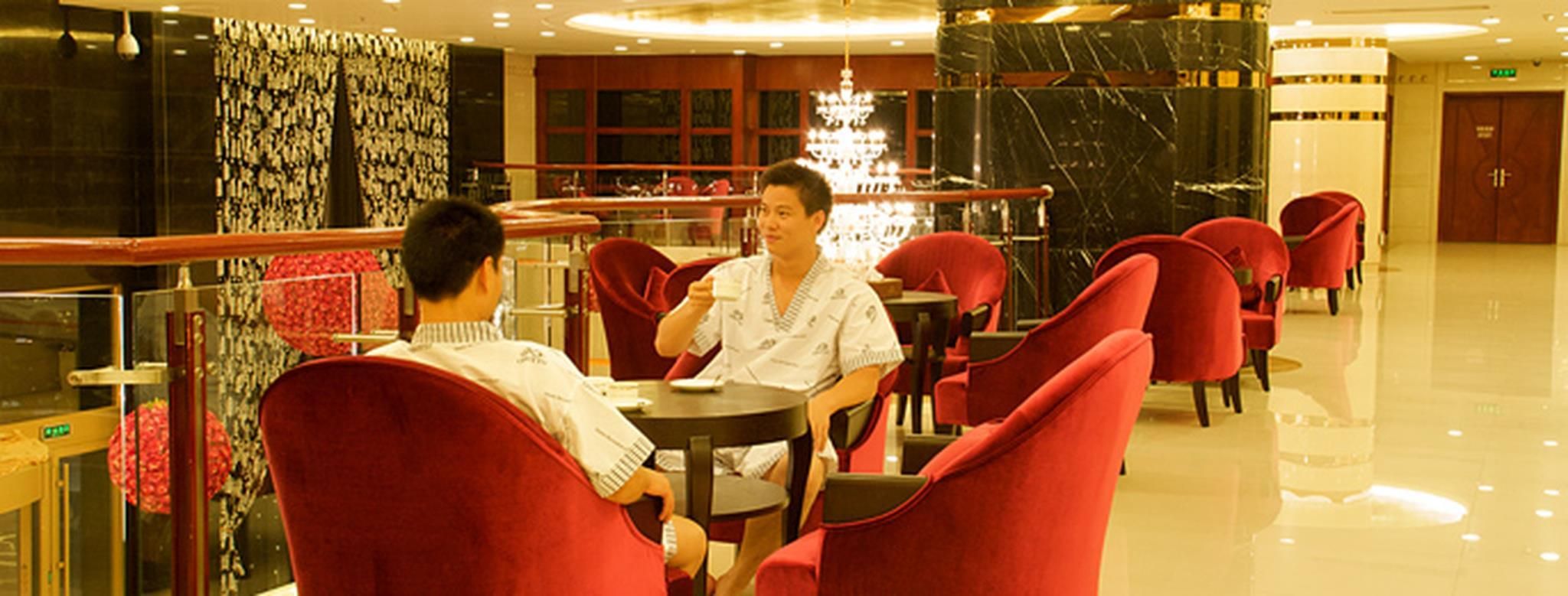 Um saguão de hotel com cadeiras vermelhas, um lustre e piso de mármore.