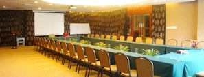 Uma sala de conferência com uma mesa comprida, cadeiras, tela de projetor e piso coberto de carpete.