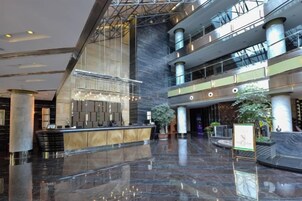 Um hall amplo com balcão de recepção, colunas imponentes e teto alto.