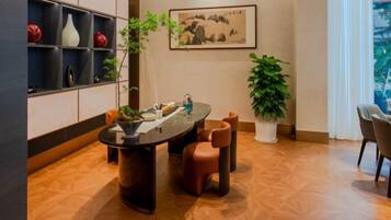 Uma sala de jantar com uma mesa redonda, cadeiras, uma planta em vaso e um quadro na parede.