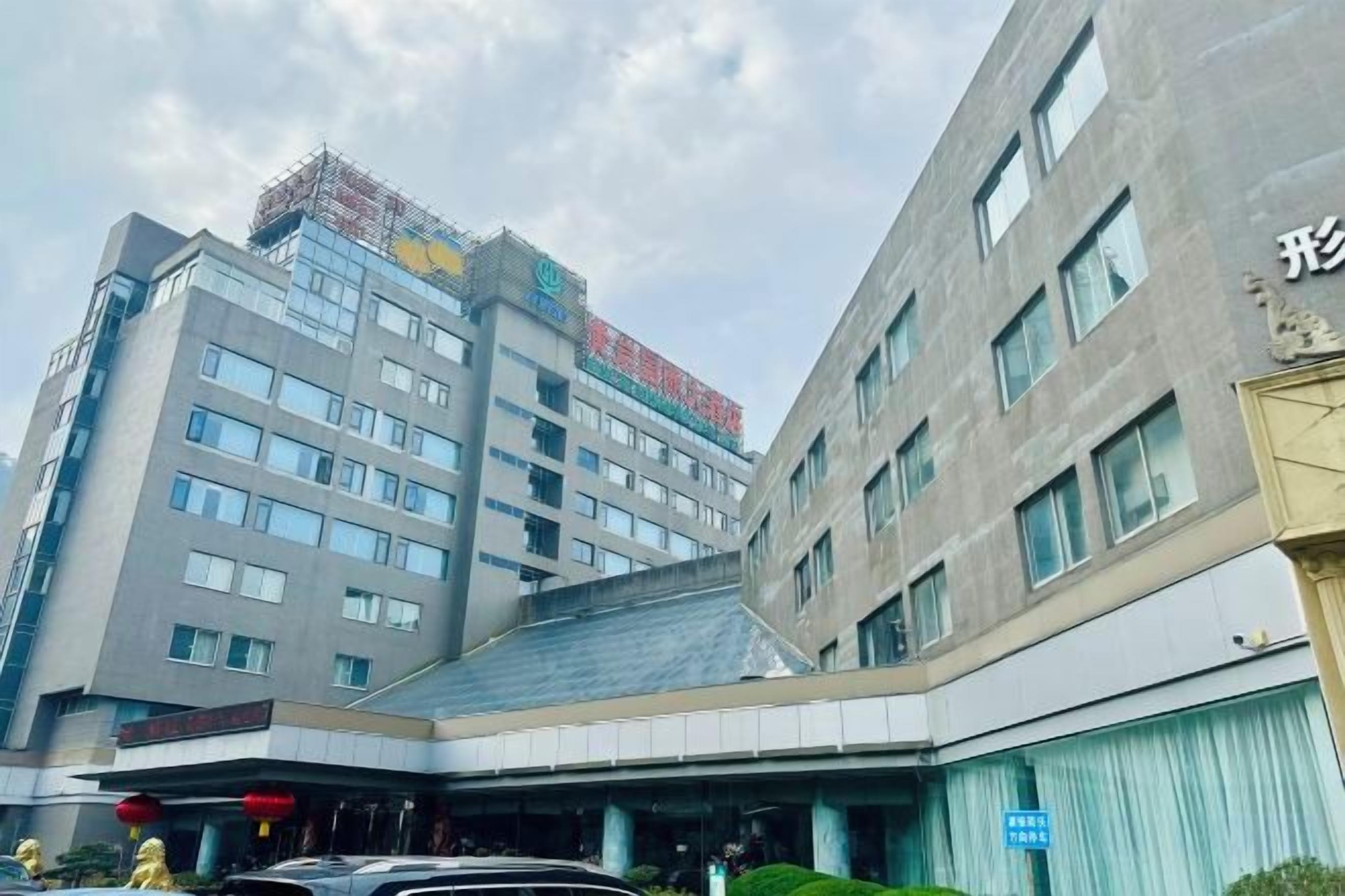 Hotel com vários andares e design arquitetônico moderno, com entrada destacada e área de estacionamento.