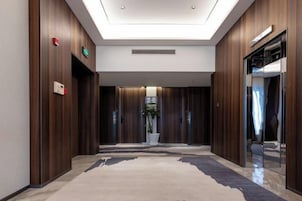 Um saguão de hotel moderno com uma planta central, painéis de madeira e piso carpeteado.