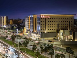 Um hotel moderno com um grande letreiro 'ibis HOTEL', rodeado por palmeiras e ruas movimentadas.