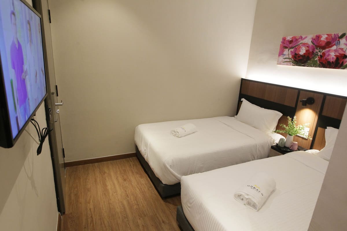 Quarto de hotel com duas camas, uma televisão na parede e um quadro sobre as camas.